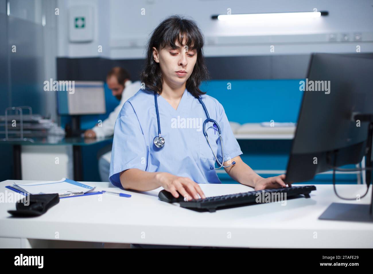Young medical assistant works on computer at desk. Working late in the ...