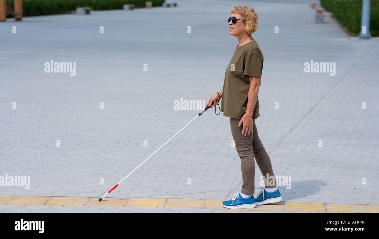 An elderly blind woman walks with a cane along a tactile tile Stock ...