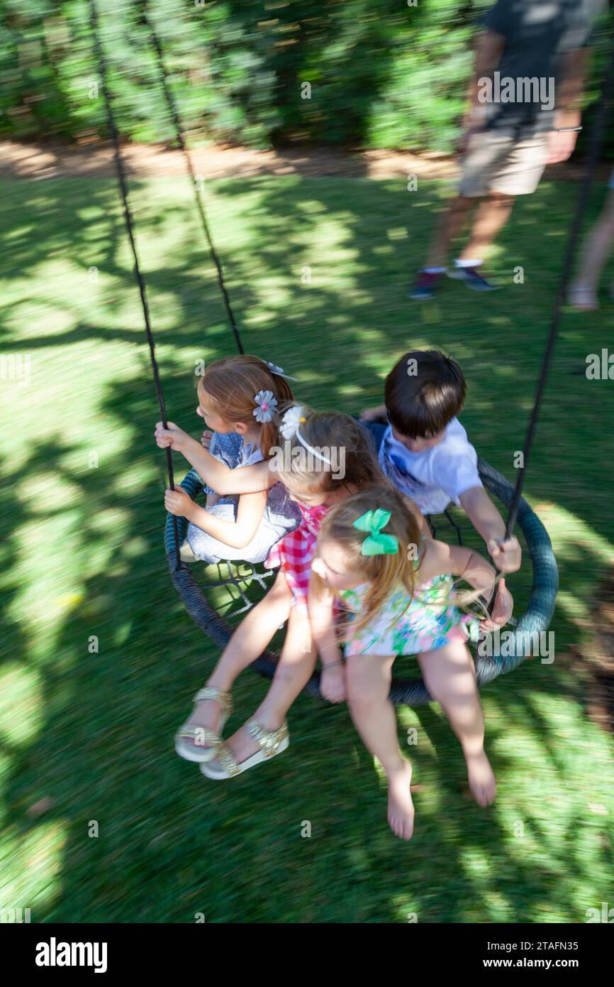 Group of kids ride together on a round rope swing in the backyard ...