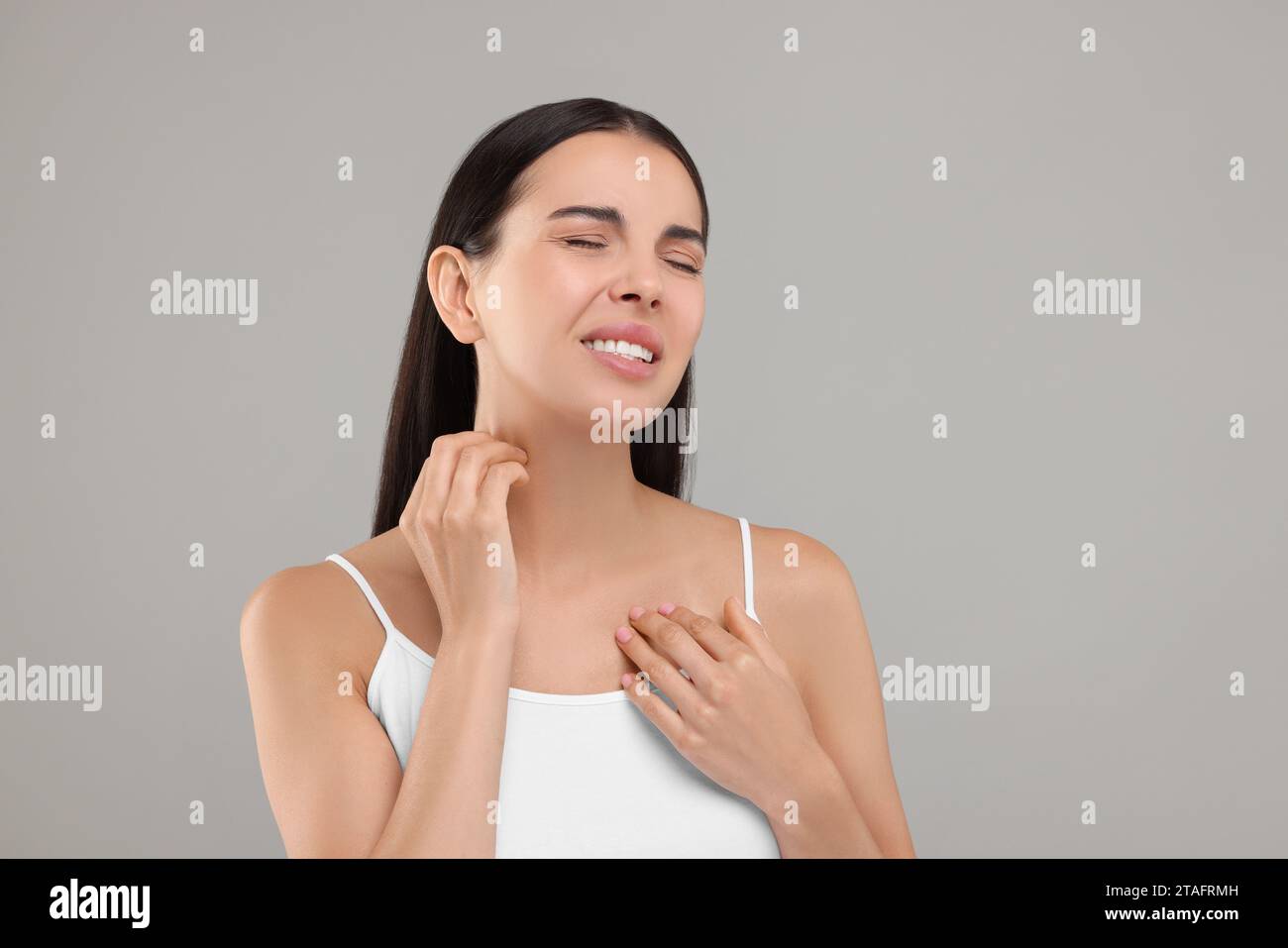 Suffering from allergy. Young woman scratching her neck on light grey ...
