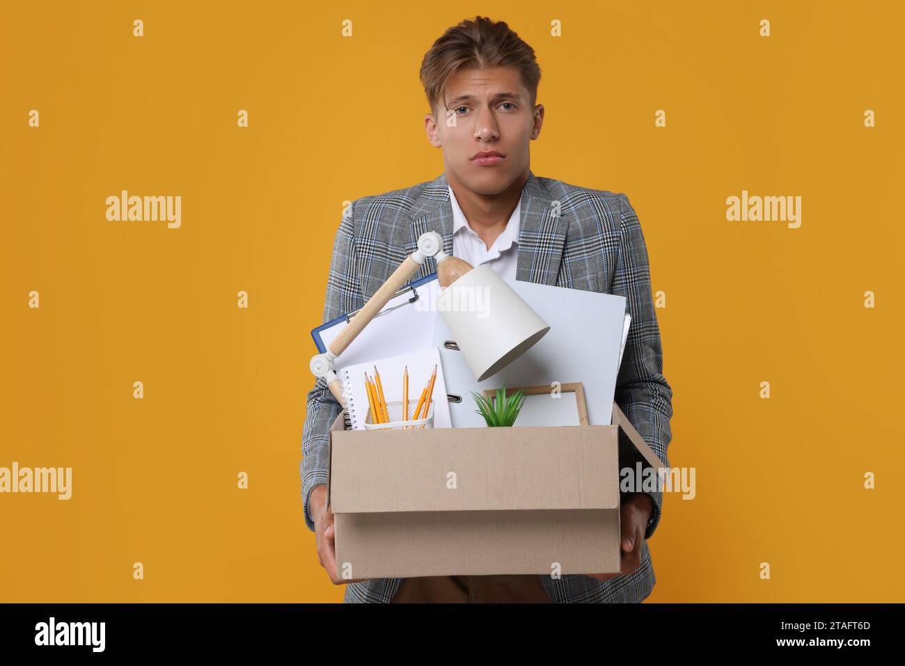 Unemployed young man with box of personal office belongings on orange ...