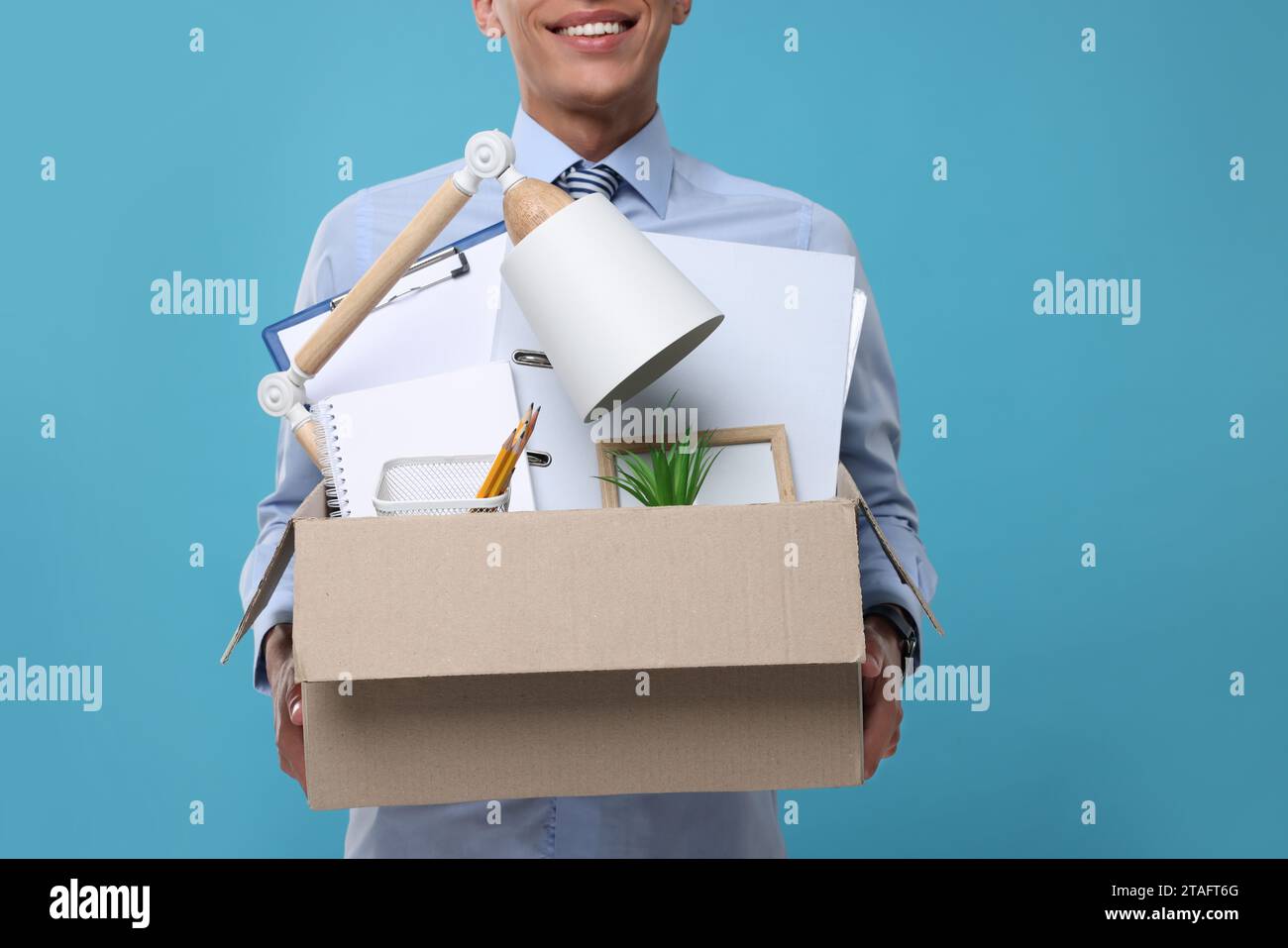 Unemployed young man with box of personal office belongings on light ...