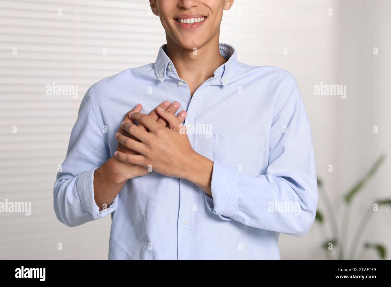 Thank you gesture. Grateful man with hands on chest indoors, closeup ...