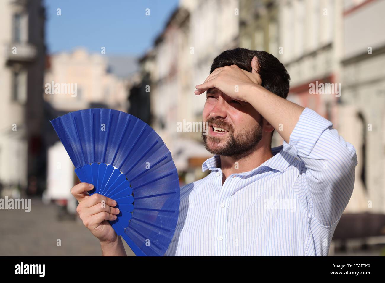 Man with hand fan suffering from heat outdoors Stock Photo - Alamy