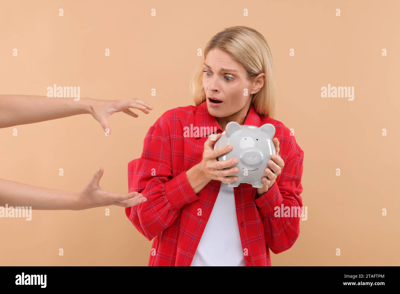 Scammer taking piggy bank from scared woman on beige background. Be ...