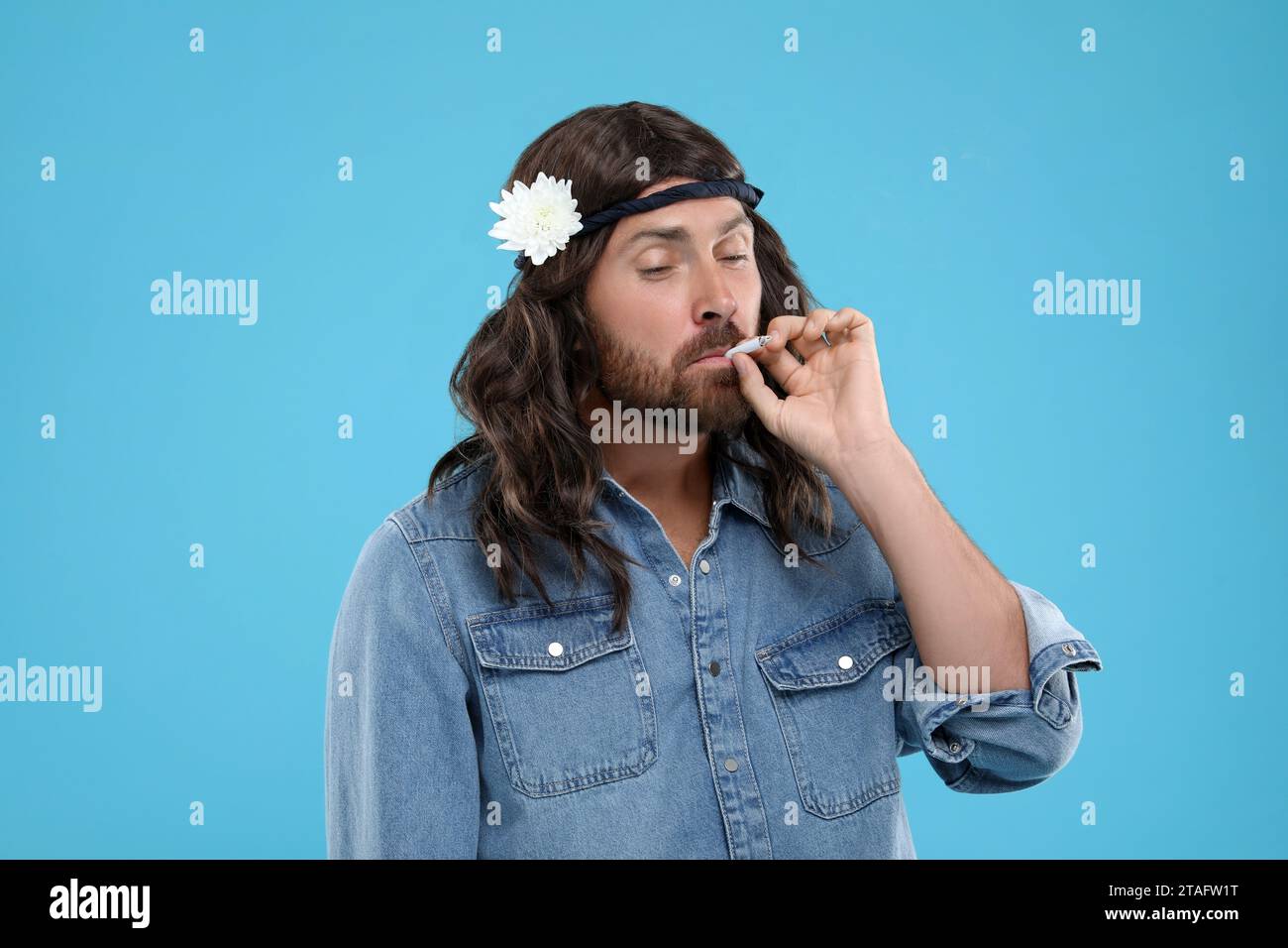 Stylish hippie man smoking cigarette on light blue background Stock ...