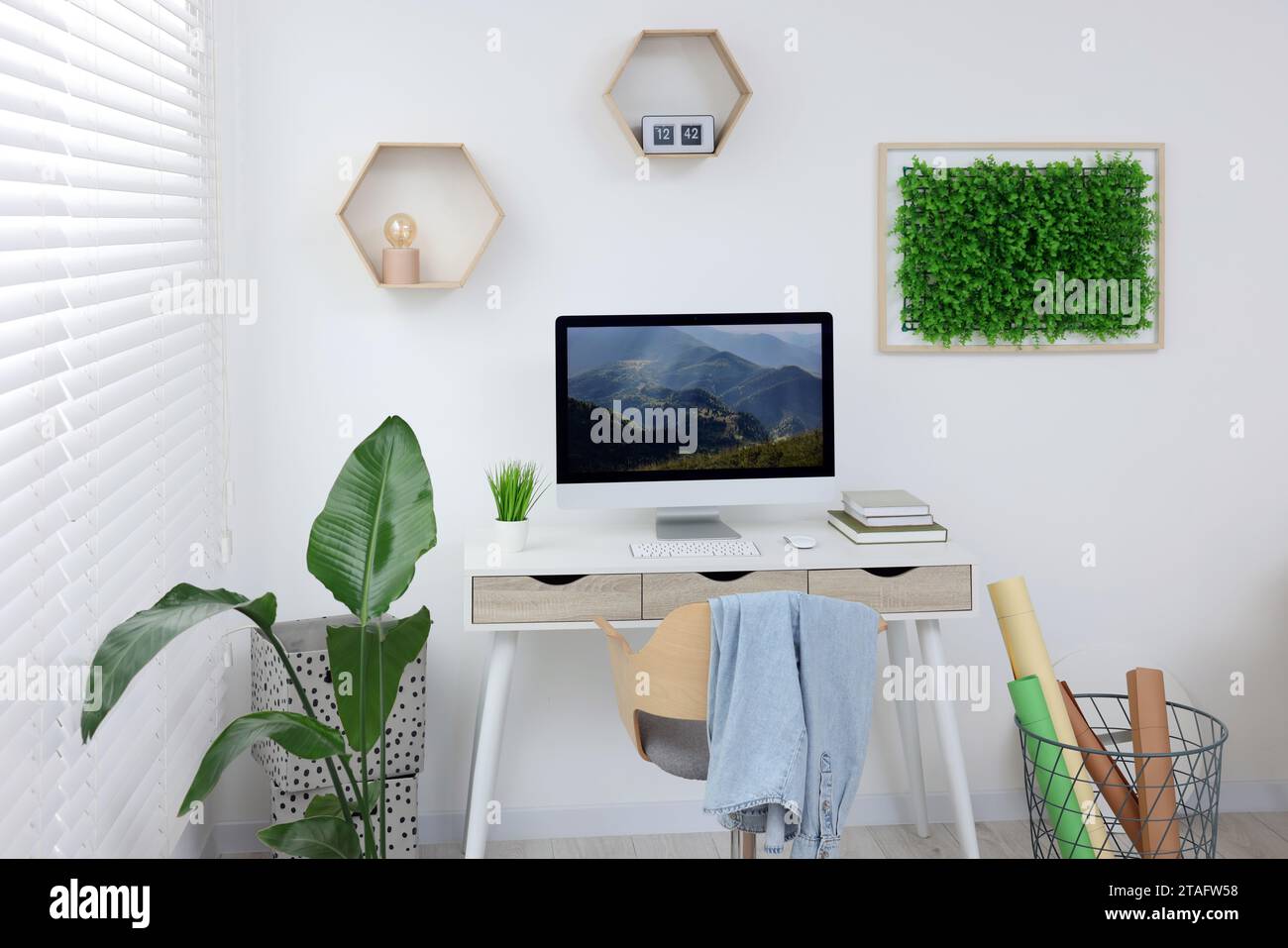 Green artificial plant wall panel and desk with computer in light room ...