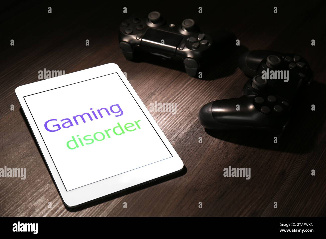 Tablet with phrase Gaming Disorder and gamepads on wooden table ...