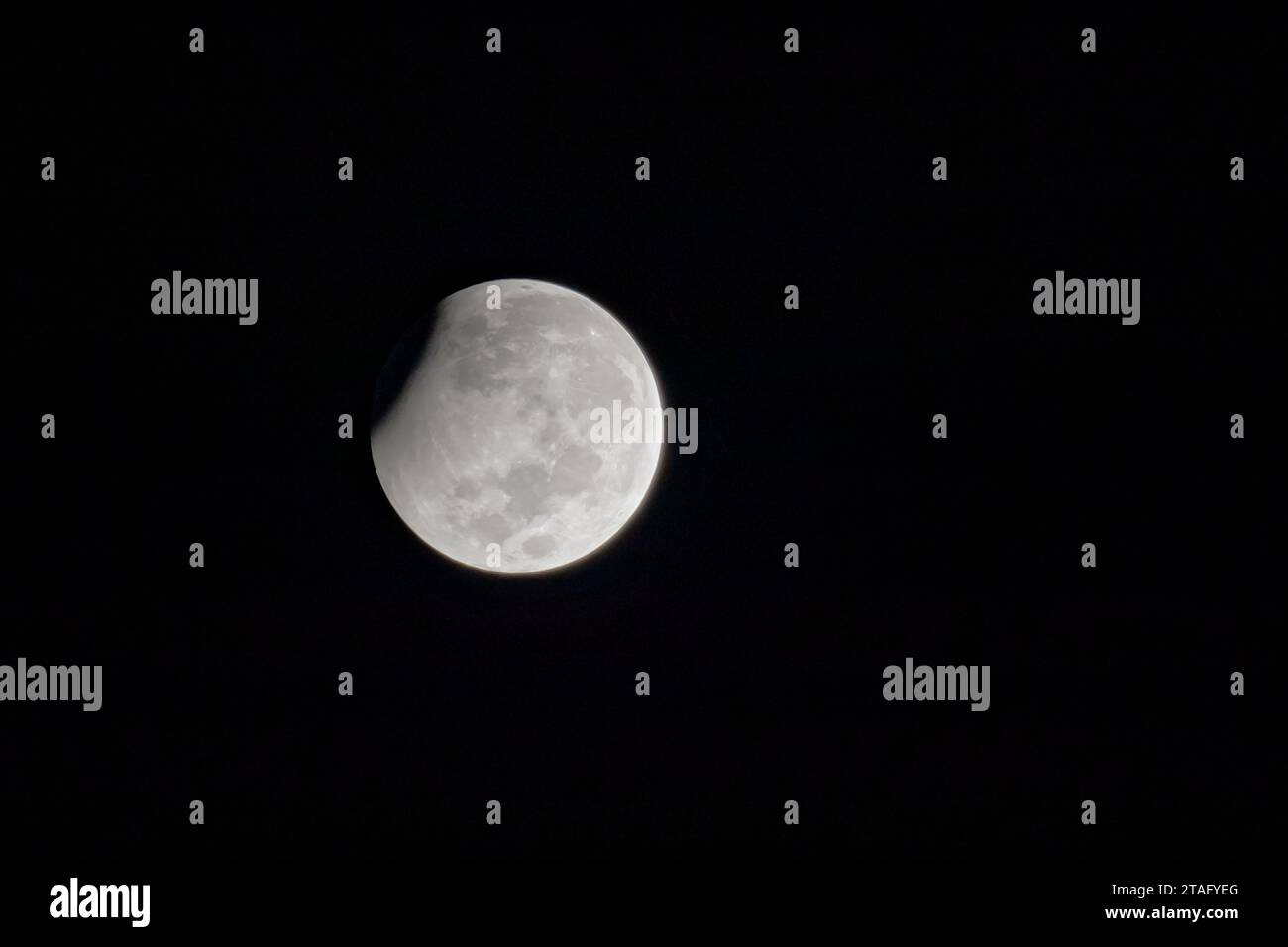 Full moon rising above horizon. Distant tree line along slope of the ...