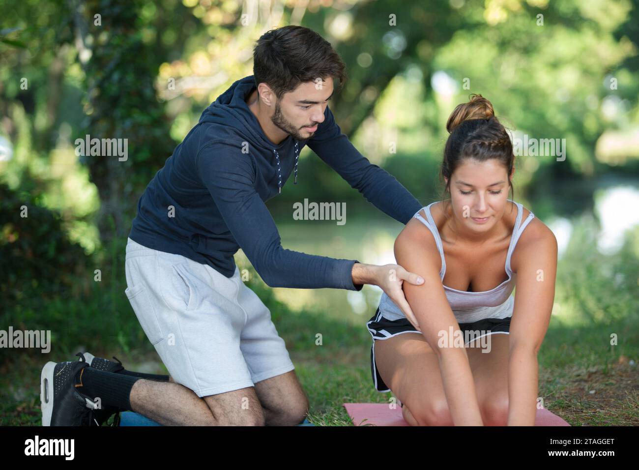 personal trainer helping female client stretching in park Stock Photo ...