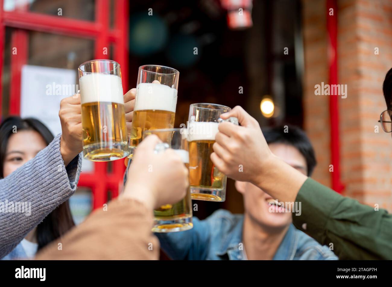 Group of cheerful young Asian friends are cheering, toasting, clinking, or enjoying beer at a ...