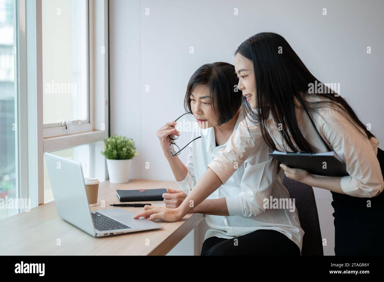 A beautiful young Asian businesswoman is helping a senior female ...