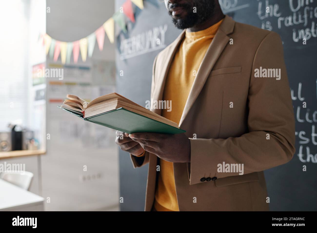African American teacher standing near the blackboard and reading ...