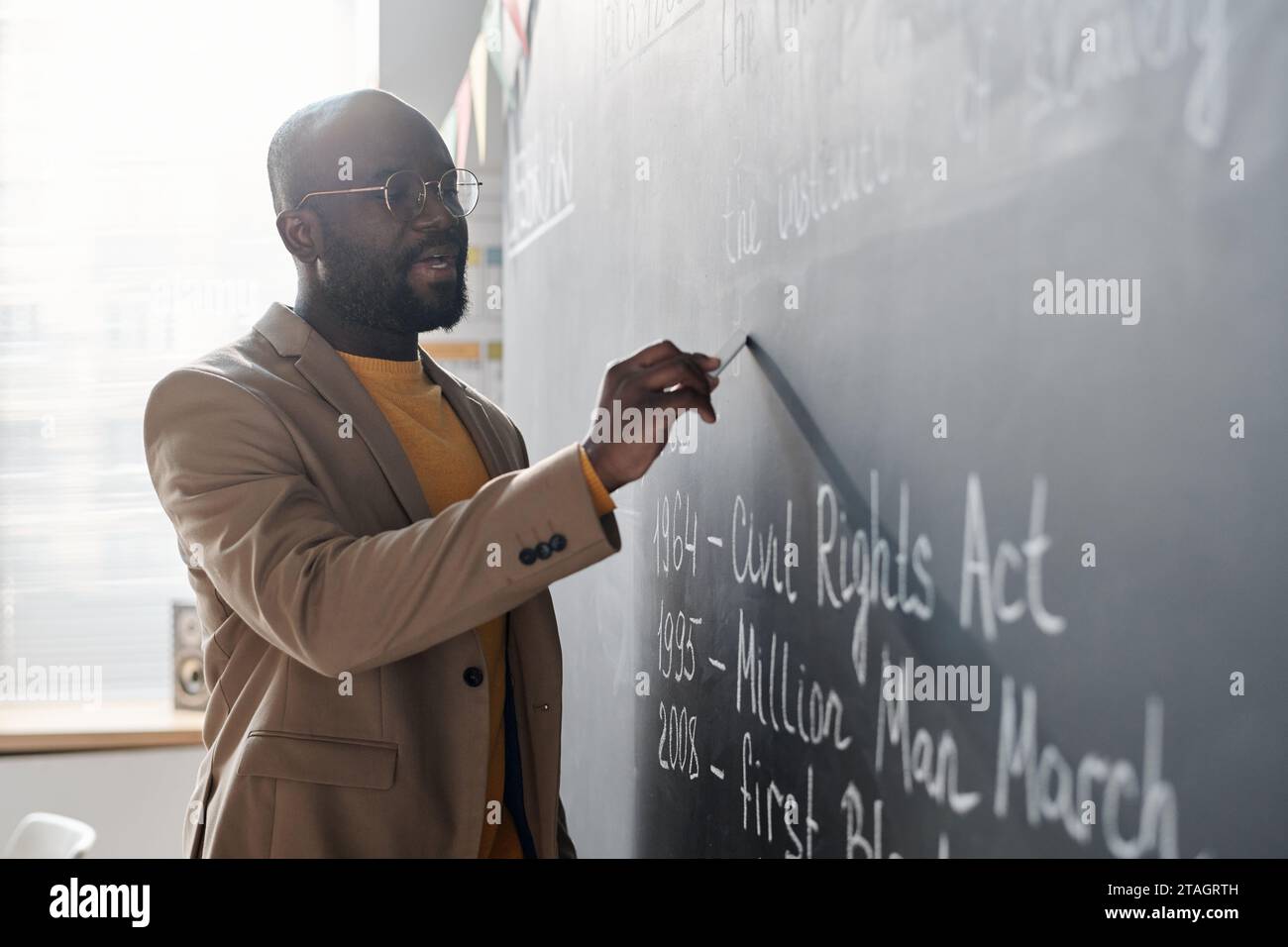 African American teacher writing information on blackboard with chalk ...
