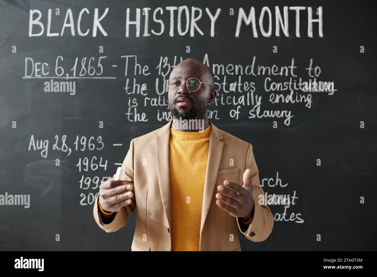African American teacher standing against the blackboard and talking ...