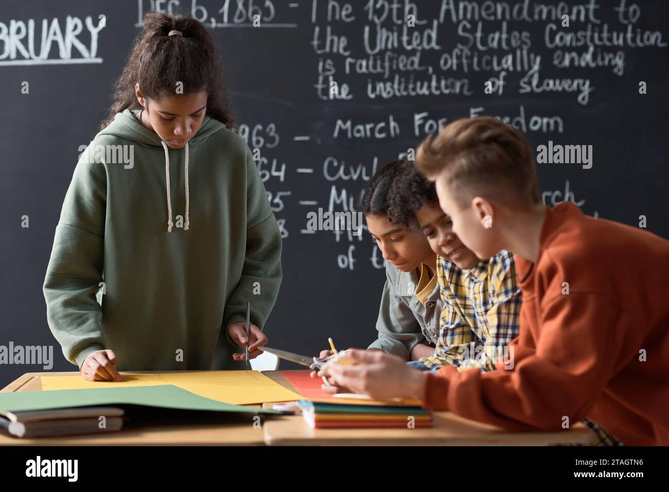 Group of school children sitting at desk and preparing report in team ...