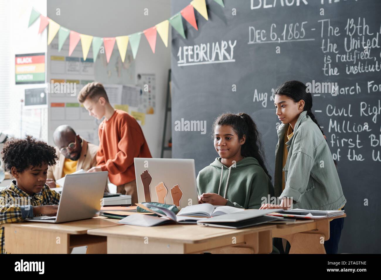 School children using computers at desk during teamwork with teacher in ...