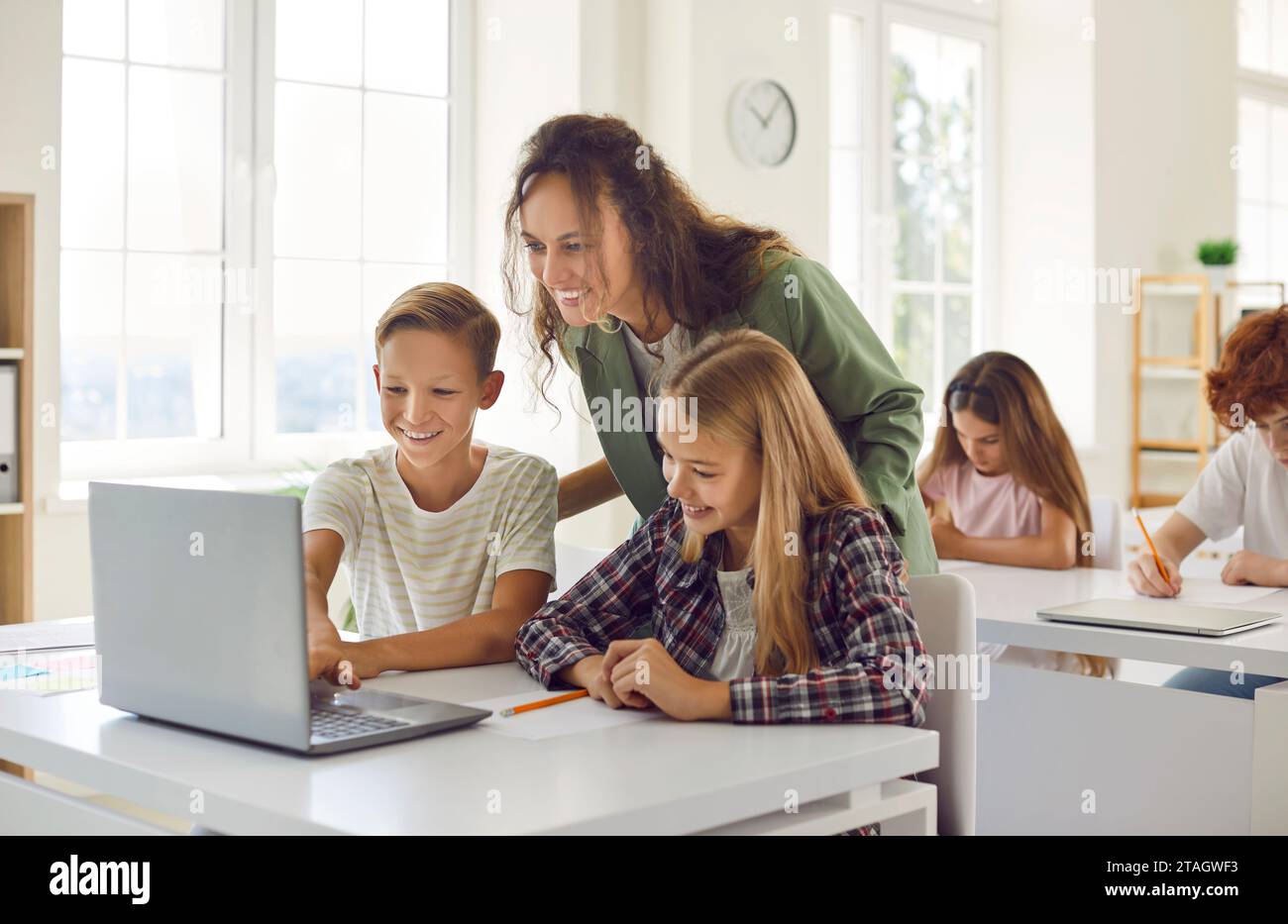 Happy smiling school children and teacher using a laptop computer in ...