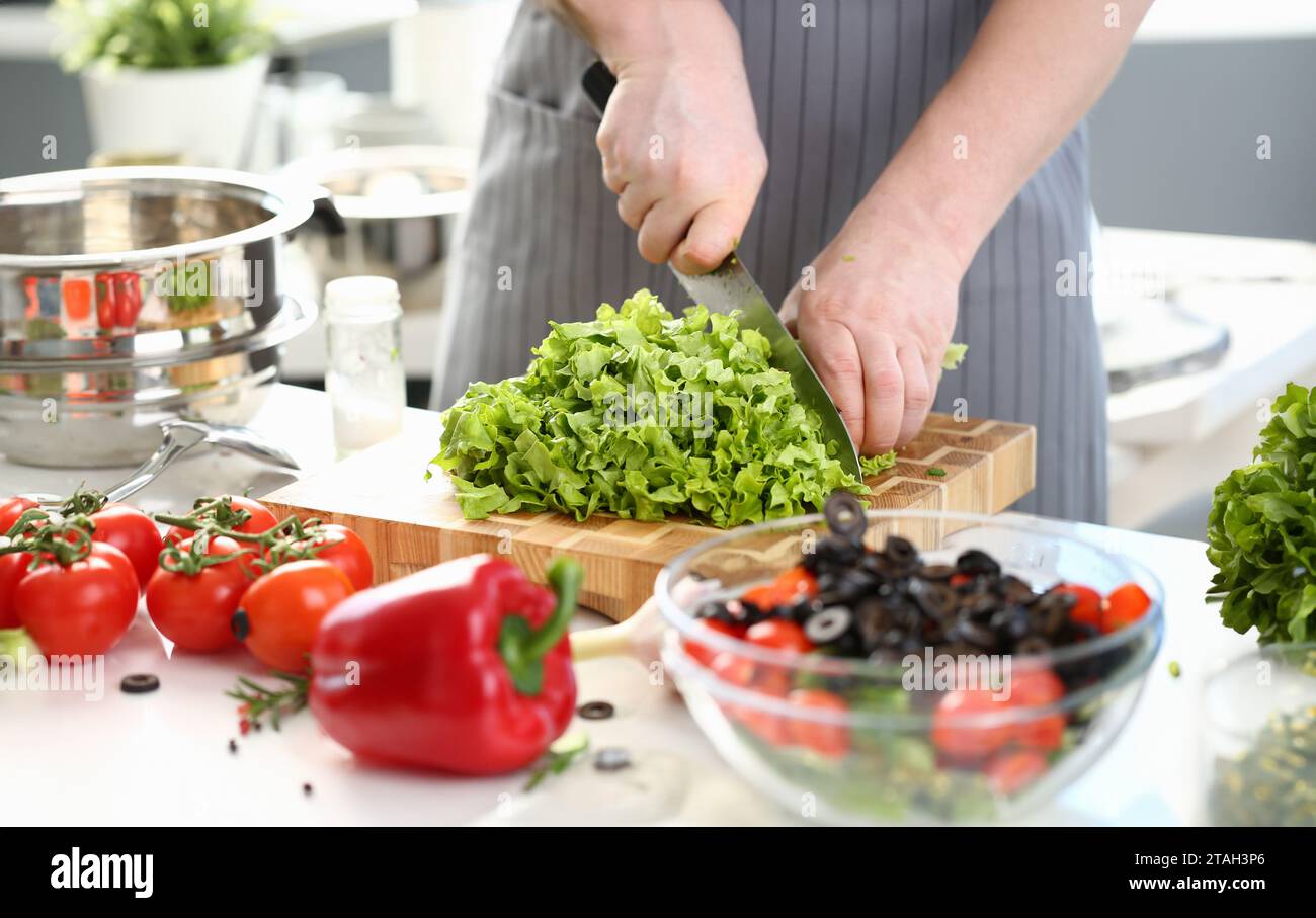 Male cook makes vegetable salad and cuts green lettuce leaves Stock ...