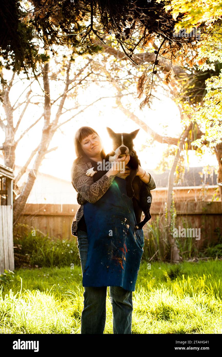 Female Artist holding small dog in backlit portrait, outdoors Stock ...