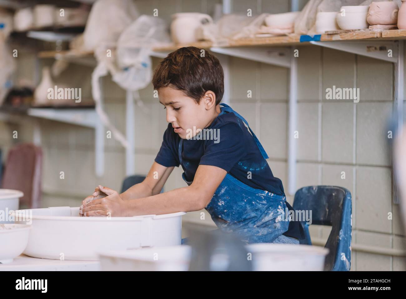 Young boy using hands to mold clay on pottery wheel Stock Photo - Alamy