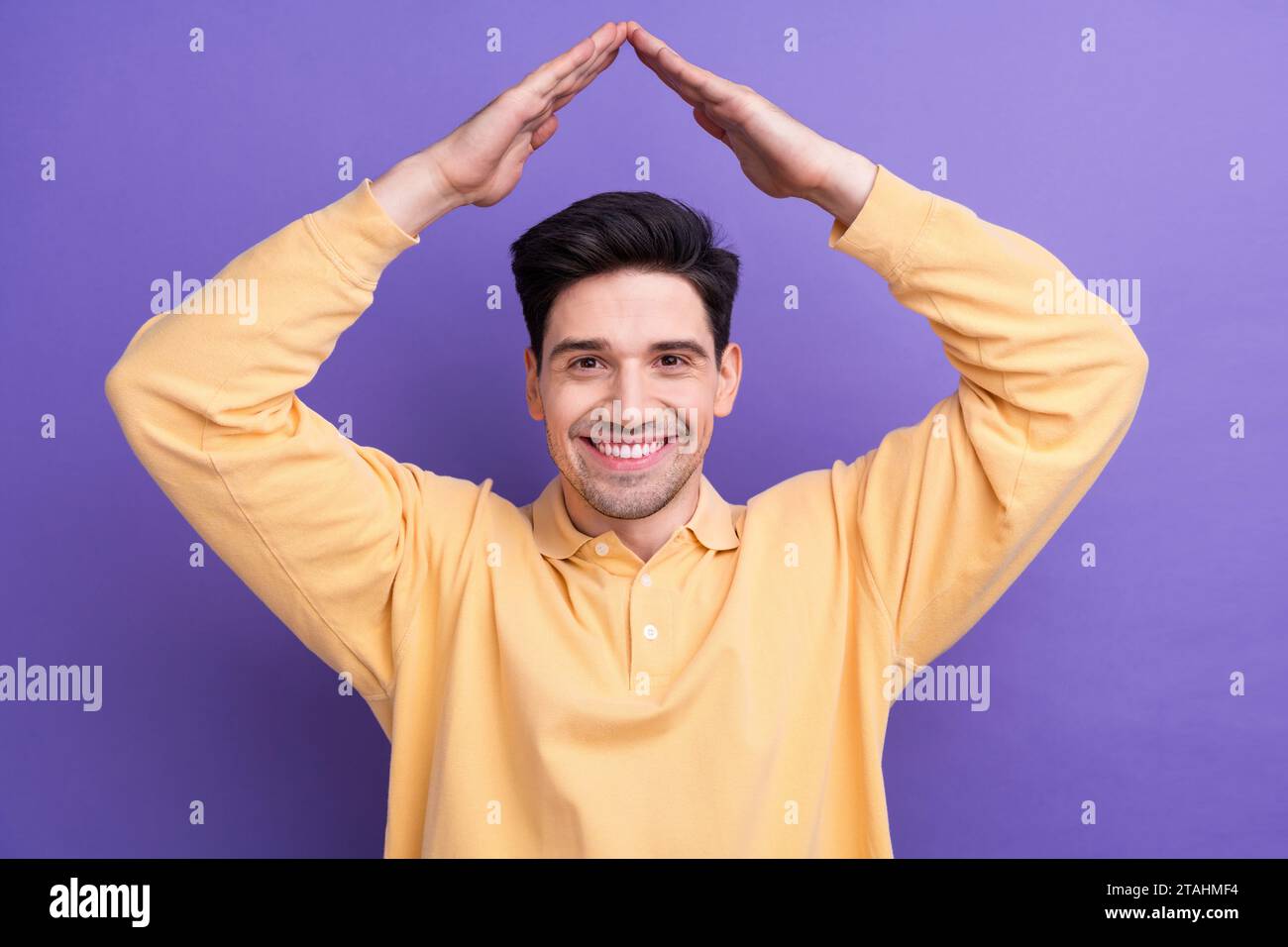 Photo portrait of nice young male raise hands showing house roof wear ...