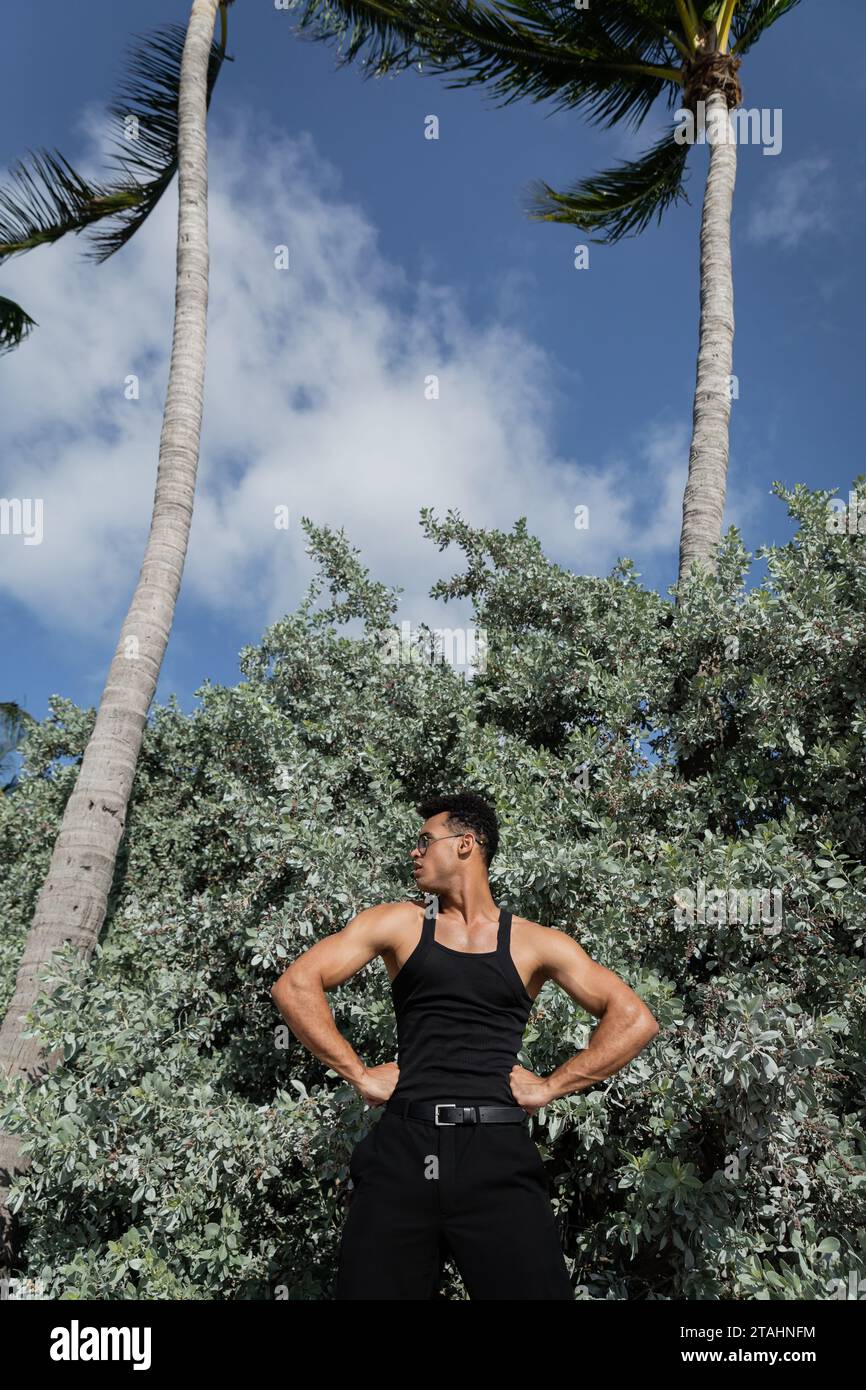 athletic cuban man in black outfit and eyeglasses near green plants ...