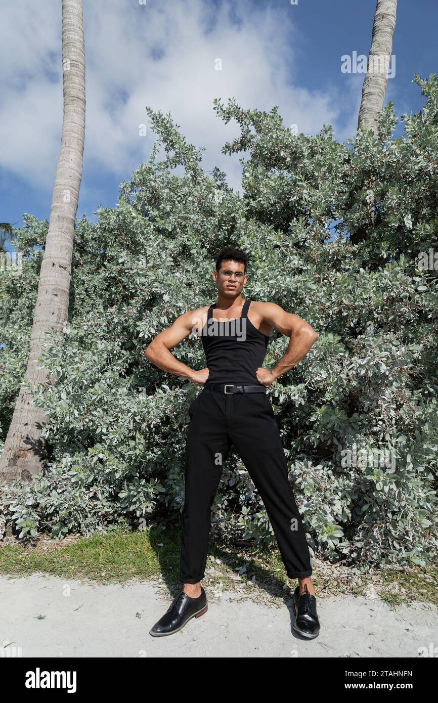 curly cuban man in black outfit and eyeglasses near green plants ...