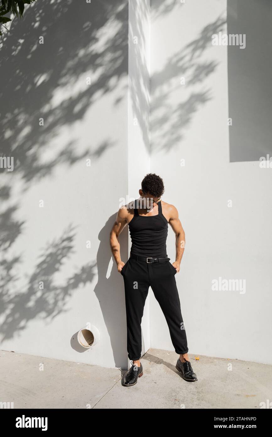 muscular young cuban man posing near white wall with shadow on urban ...