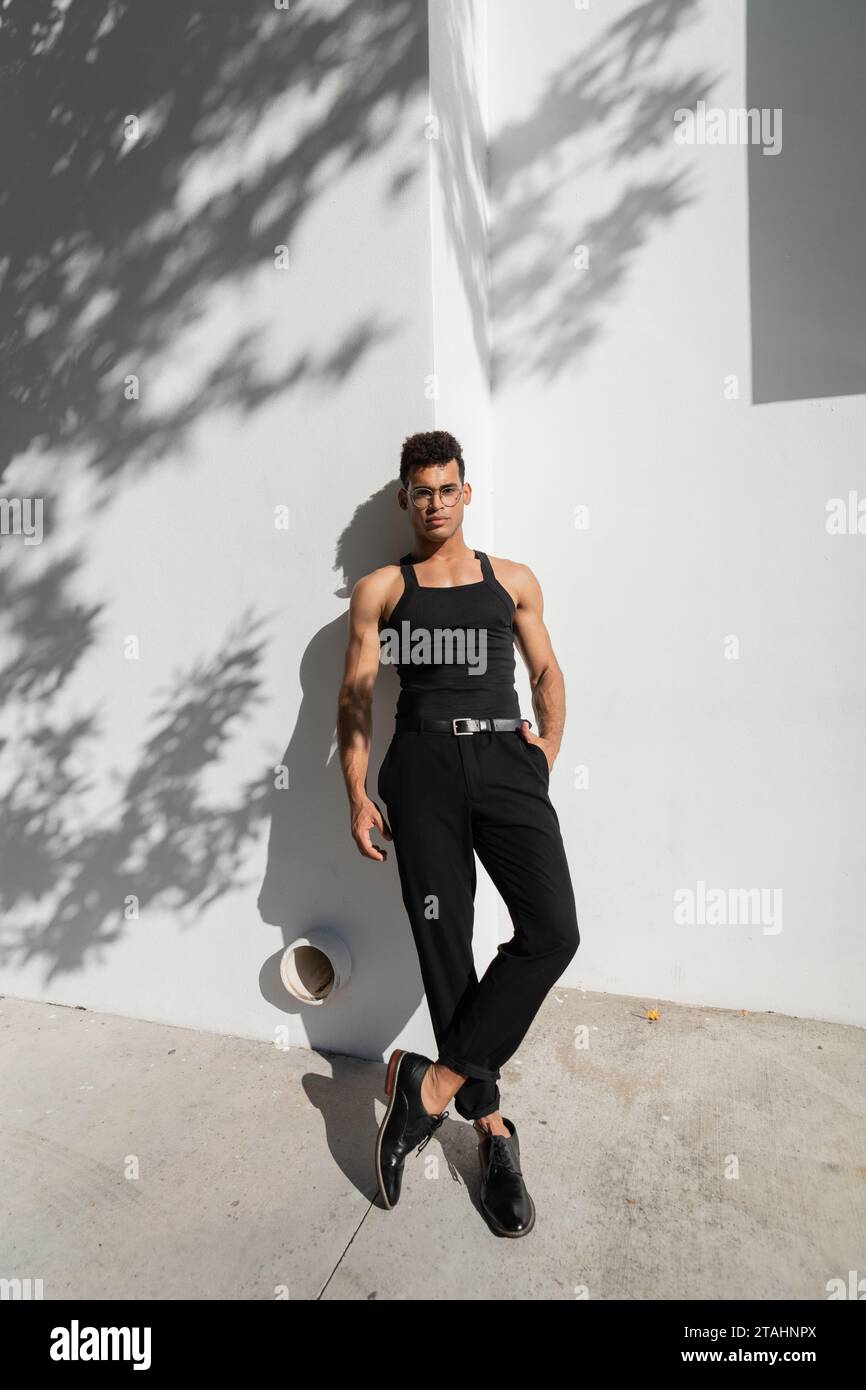 Trendy young cuban man posing near white wall with shadow on urban ...