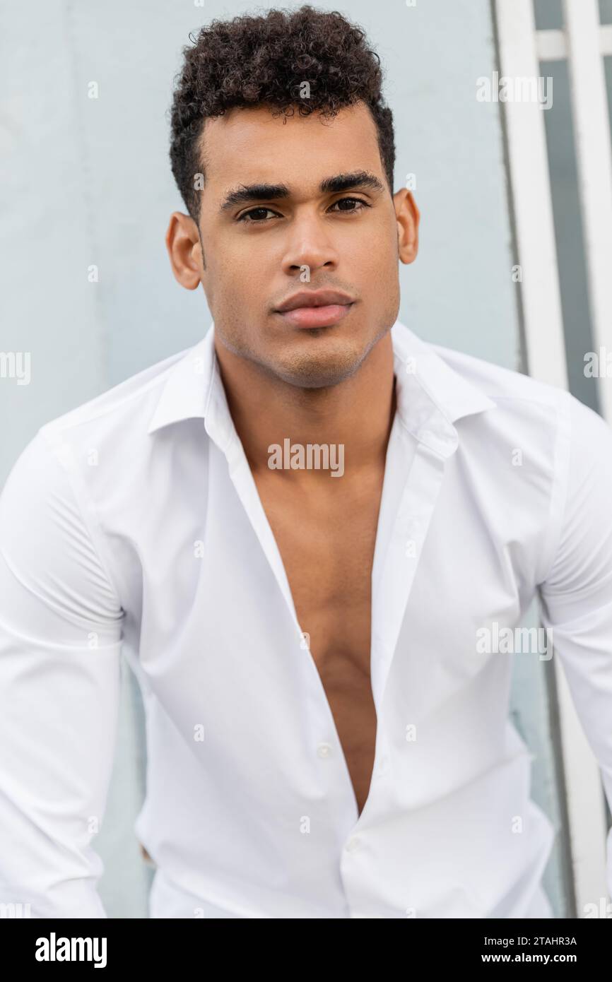 Portrait of curly and stylish cuban man in white shirt looking at ...