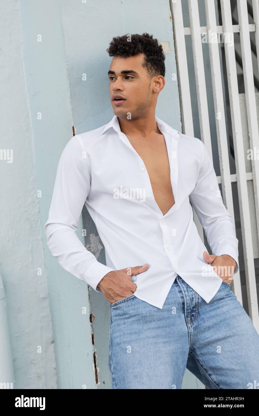 Good looking cuban man in white shirt and blue jeans posing on street ...