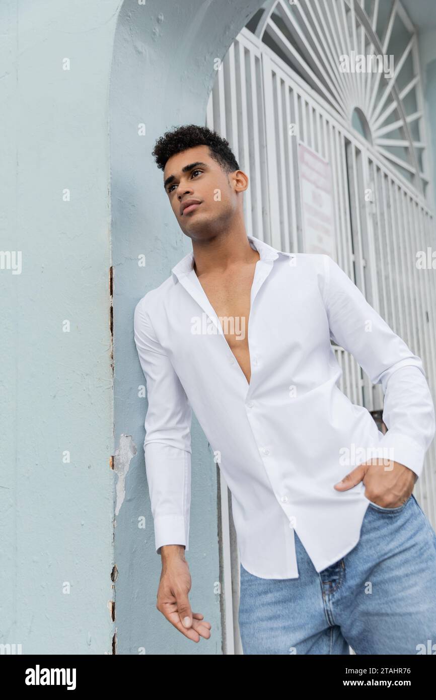 handsome and curly cuban man in stylish shirt and blue jeans posing on ...