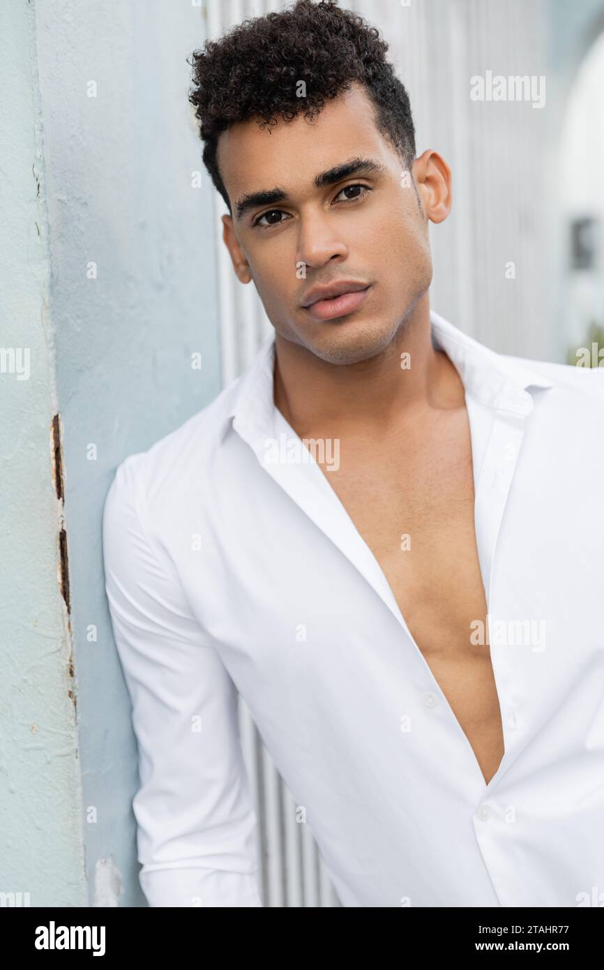 Portrait of young and curly cuban traveler in white shirt looking at ...