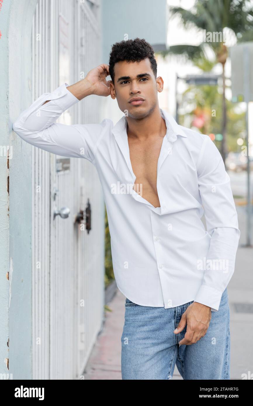 curly young cuban man in stylish shirt and blue jeans posing on street ...