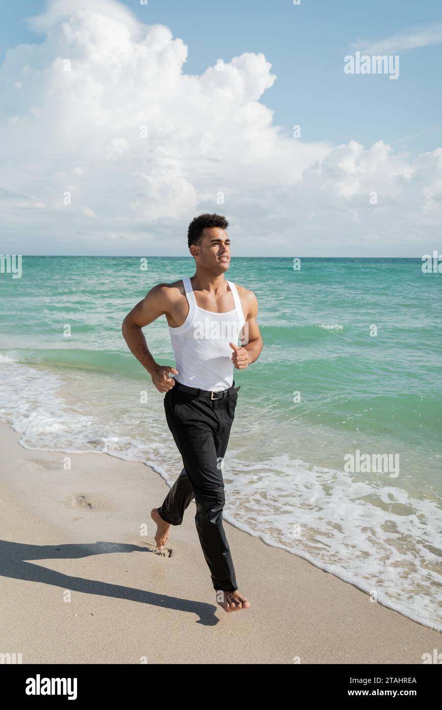 happy cuban young man running on sand near ocean water of Miami South ...