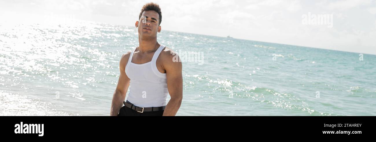 stylish young cuban man looking at camera with ocean water and sky at ...