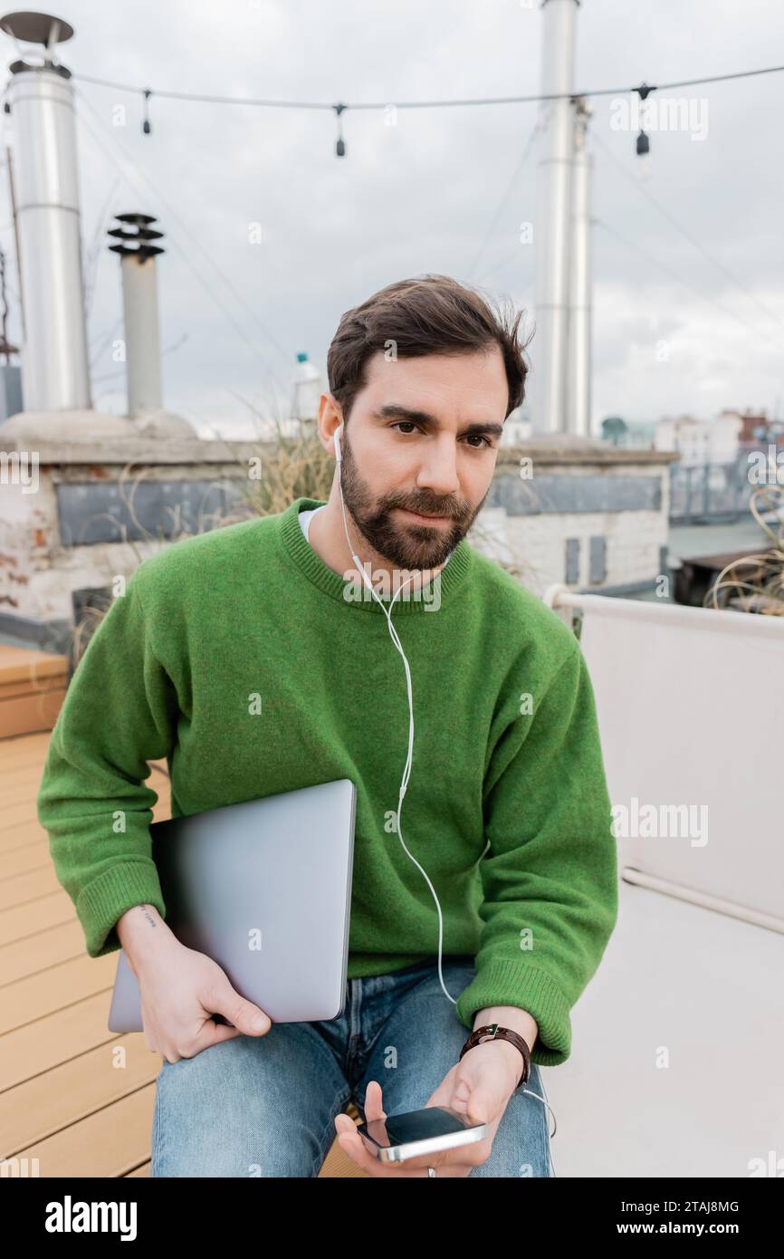 freelancer in earphones holding laptop on rooftop terrace in Vienna ...