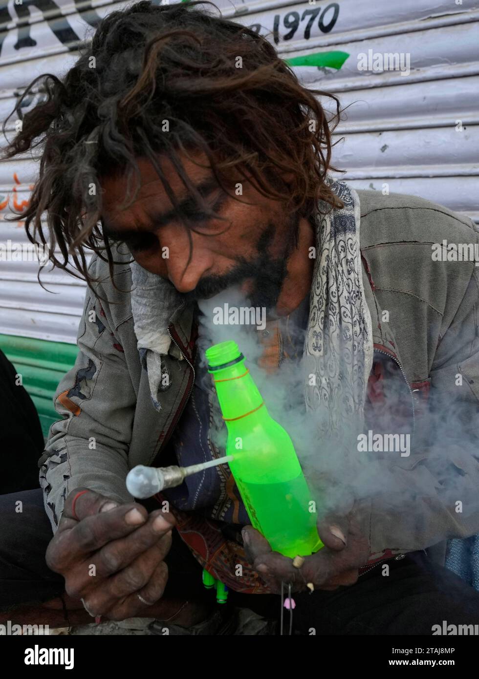 A Pakistani drug addict smokes heroin on a roadside in Karachi ...