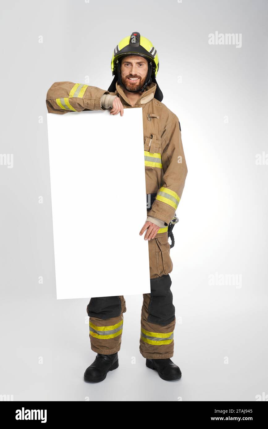 Smiling fireman in yellow helmet standing with blank banner in studio ...