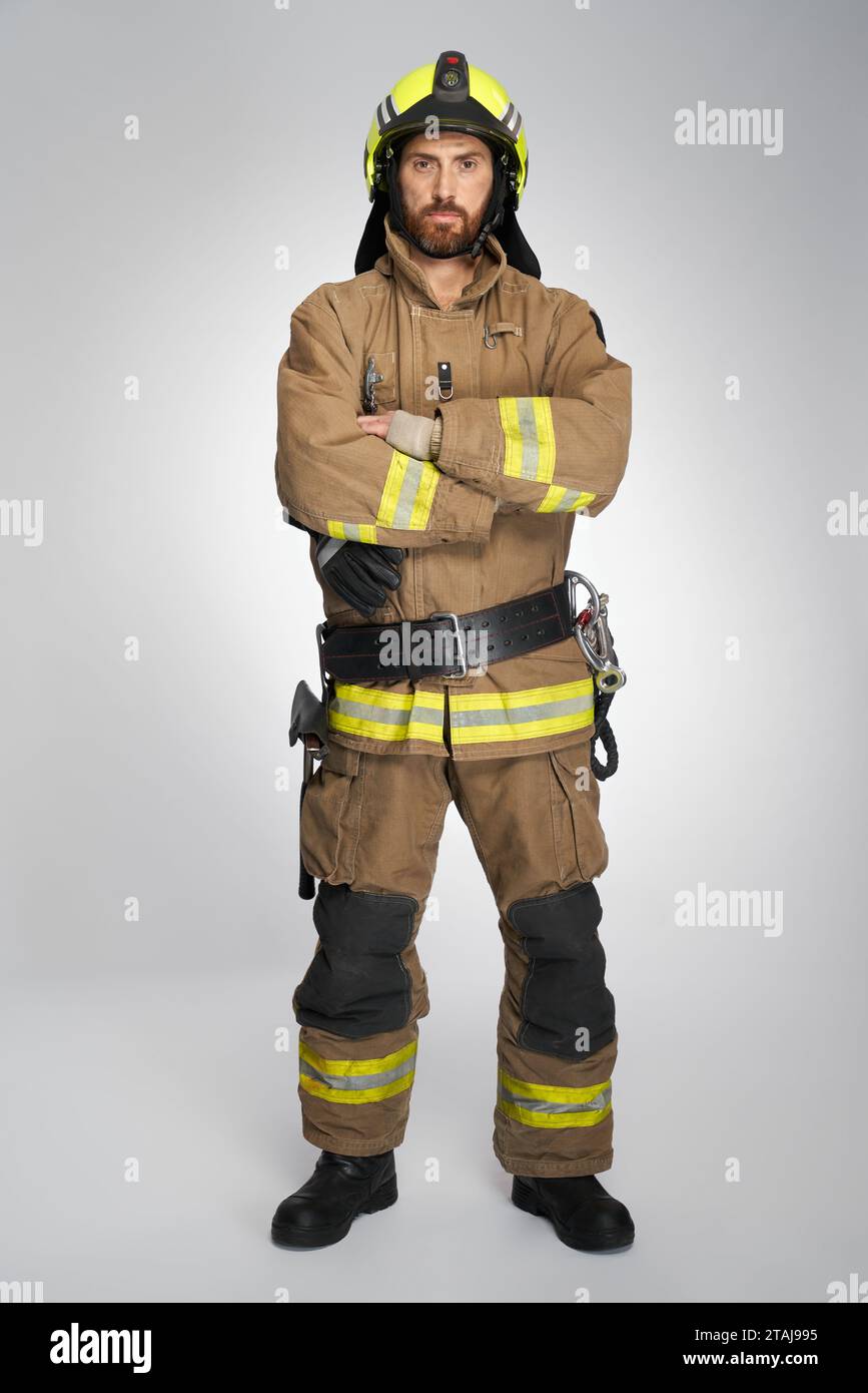 Serious male firefighter in full gear posing with crossed hands in ...