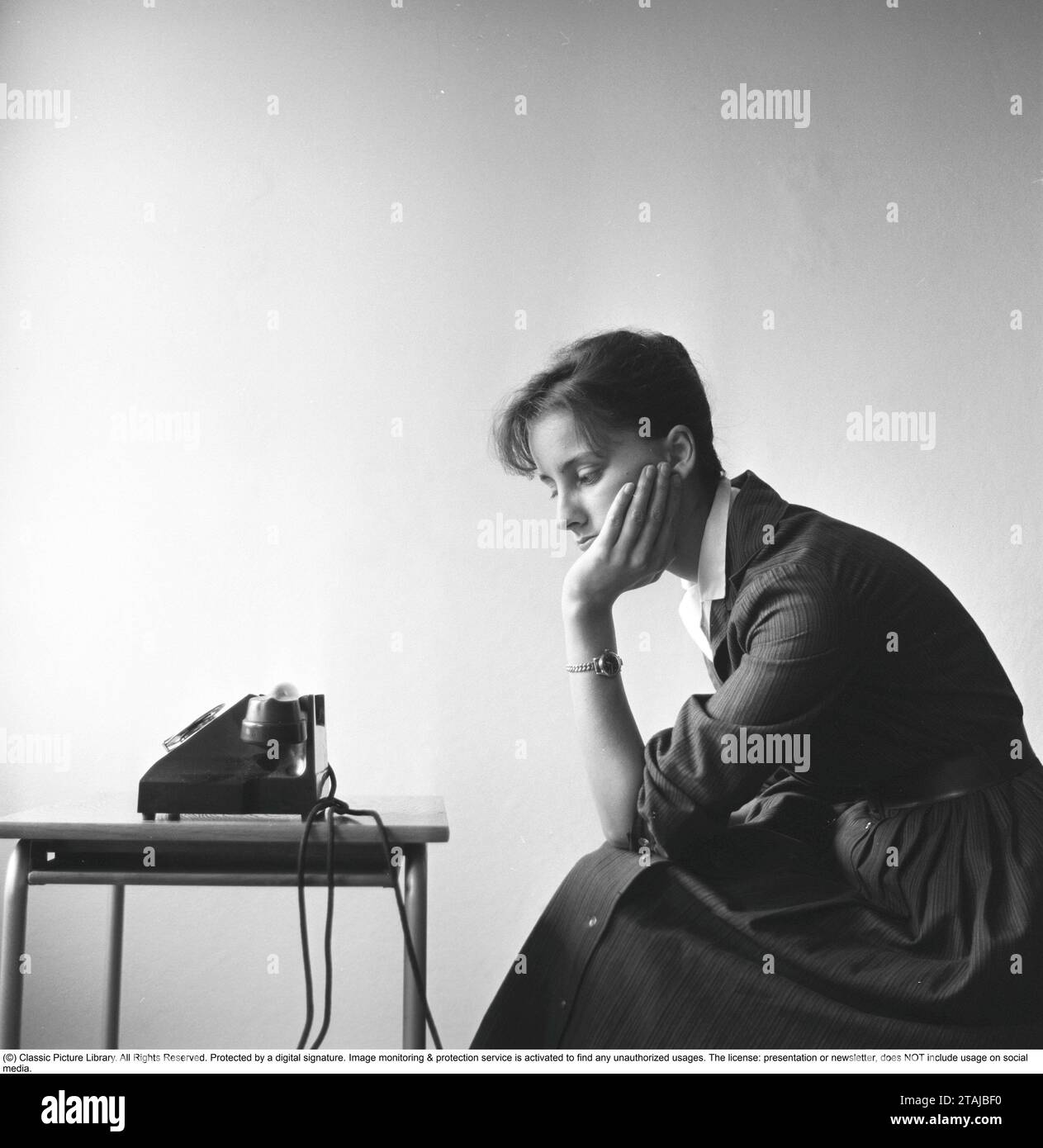 Woman in the 1950s. A young woman seen sitting by the telephone as if ...