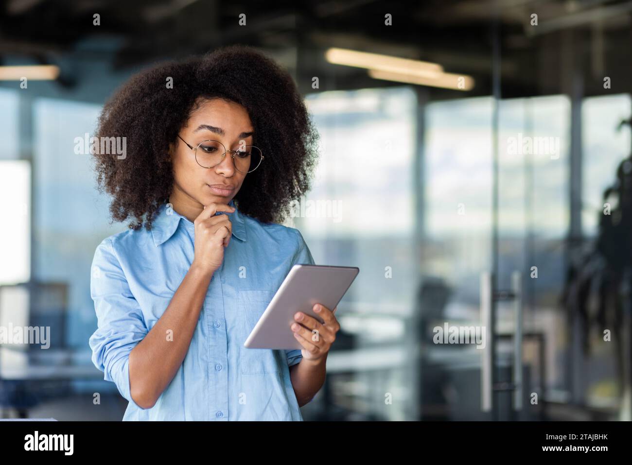 Serious thinking woman standing near window inside office ...