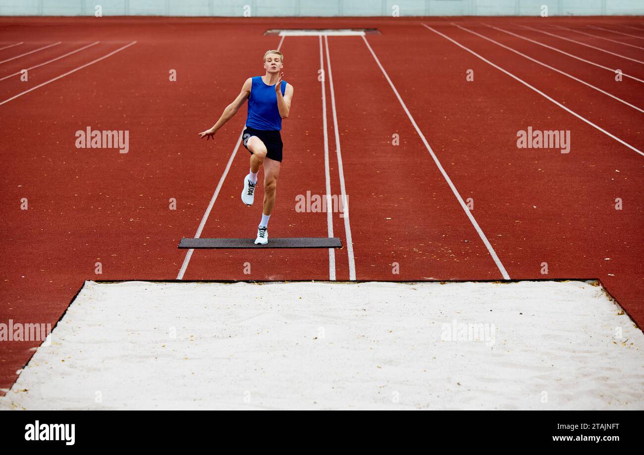 Take off. Focused runner propelling into sand pit. Young man ...