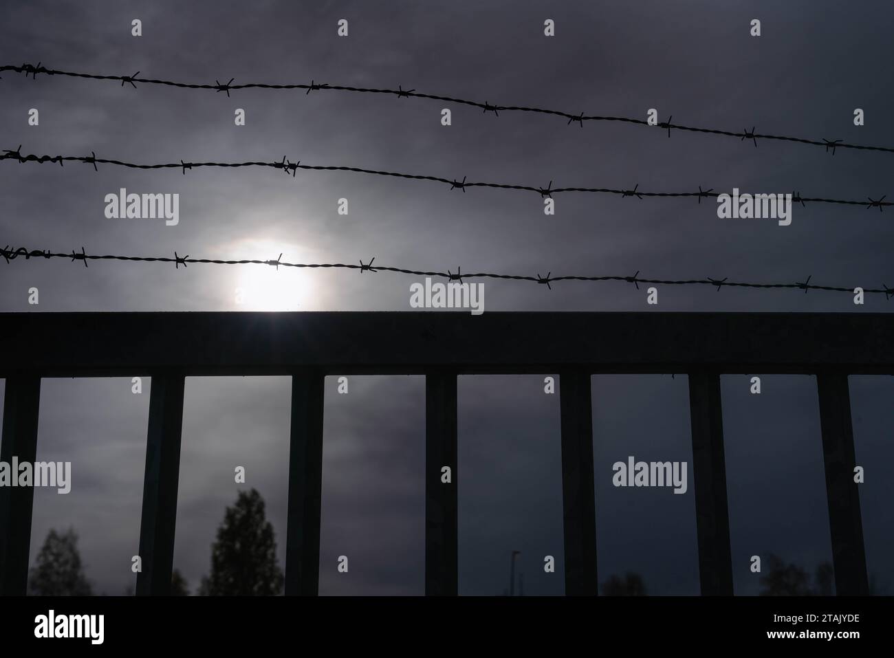 The Sun shines between high metal strong fence with barber wire above ...
