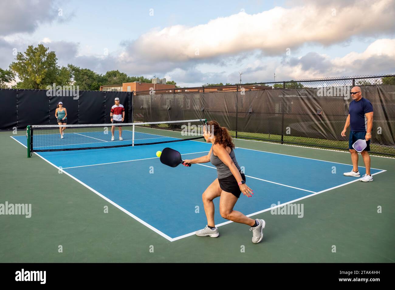 A female pickleball player returns a ball as her partner watches in a ...