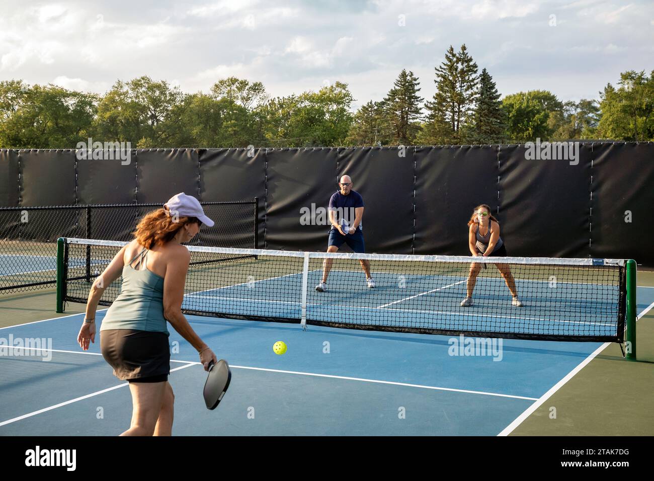 A female pickleball player returns a ball as her opponents stand at the ...