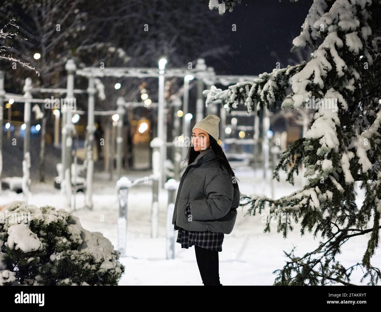 Young woman walking on walkway among snowy winter park at night against ...