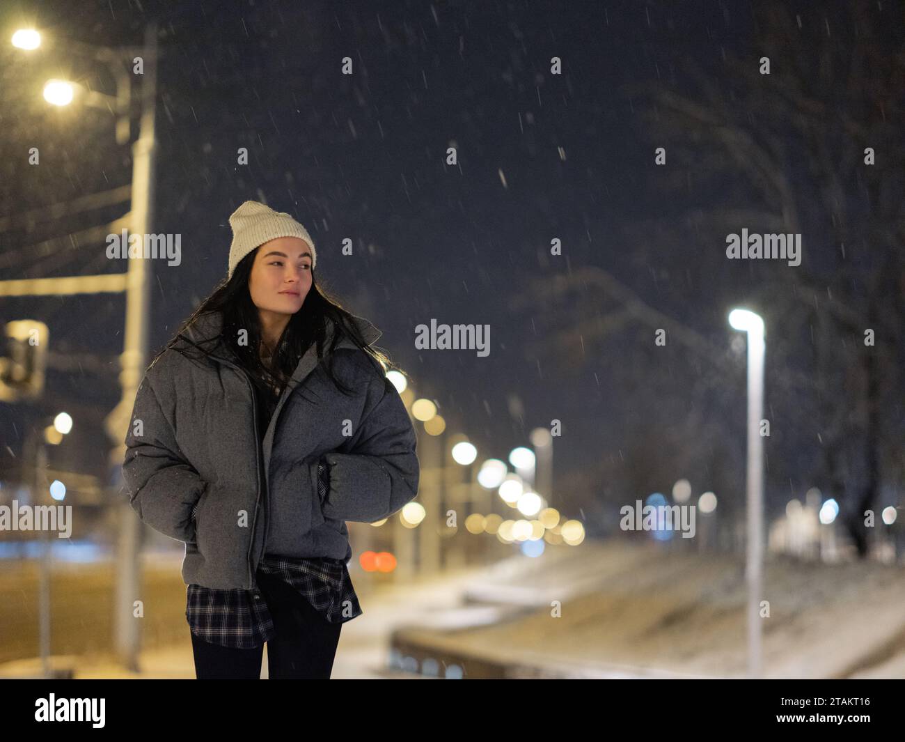 Young woman walking on walkway among snowy winter city at night against ...