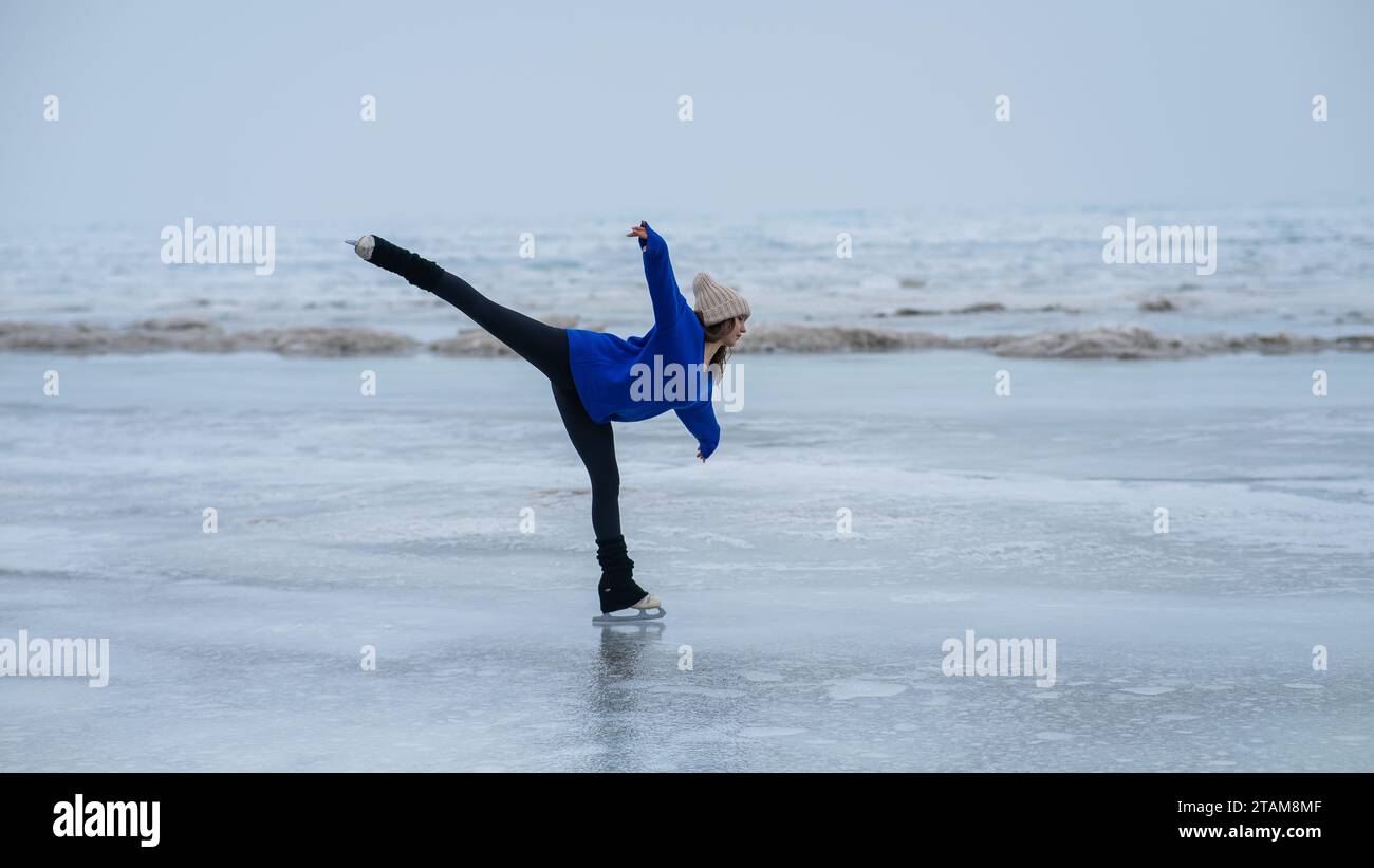 Caucasian woman in a blue sweater is skating on a frozen lake. Figure ...